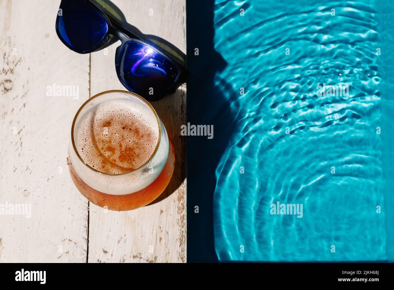 A top view of a glass of beer next to sunglasses on the pool coping ...