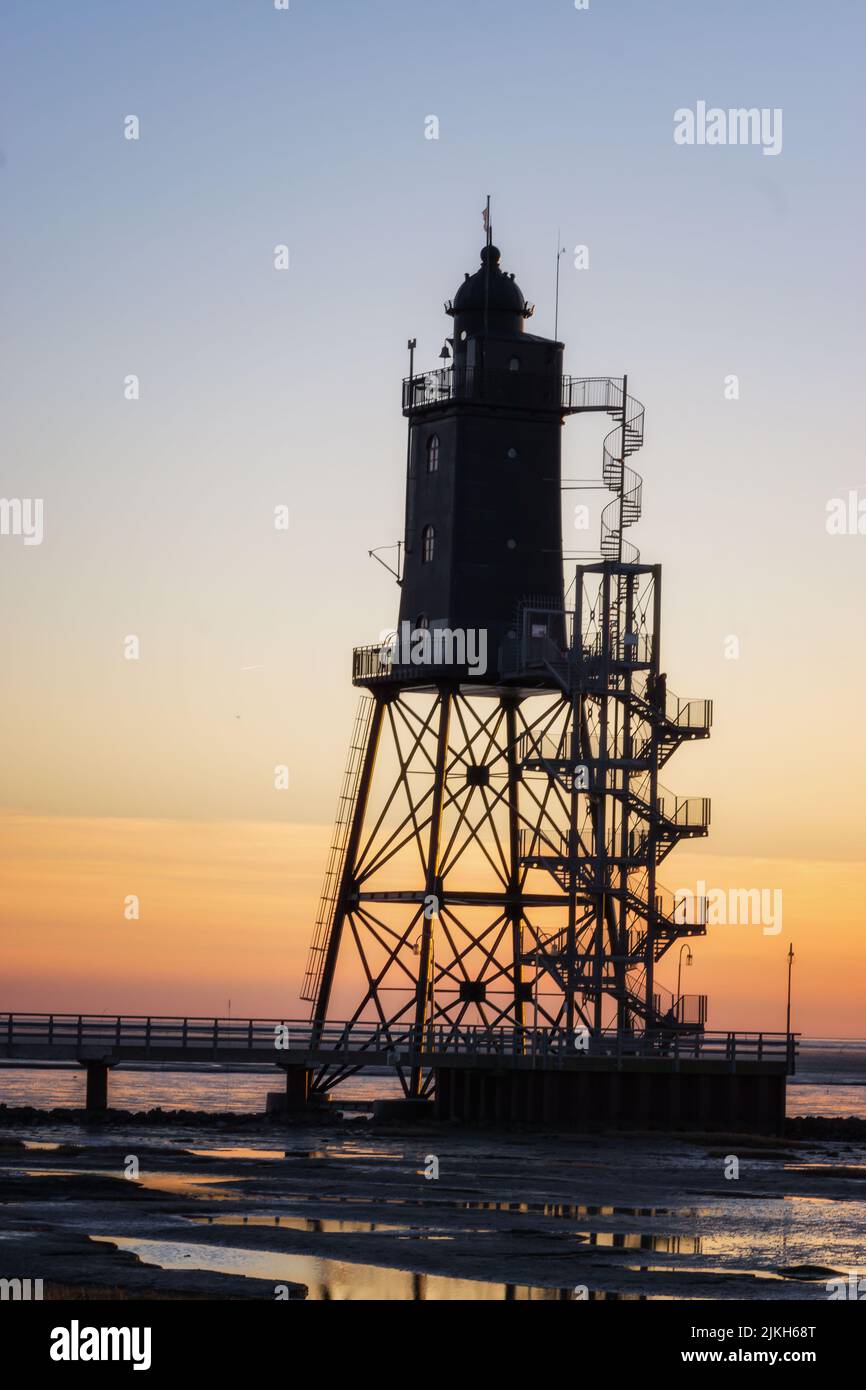 A vertical view of the historical Obereversand lighthouse during sunset ...