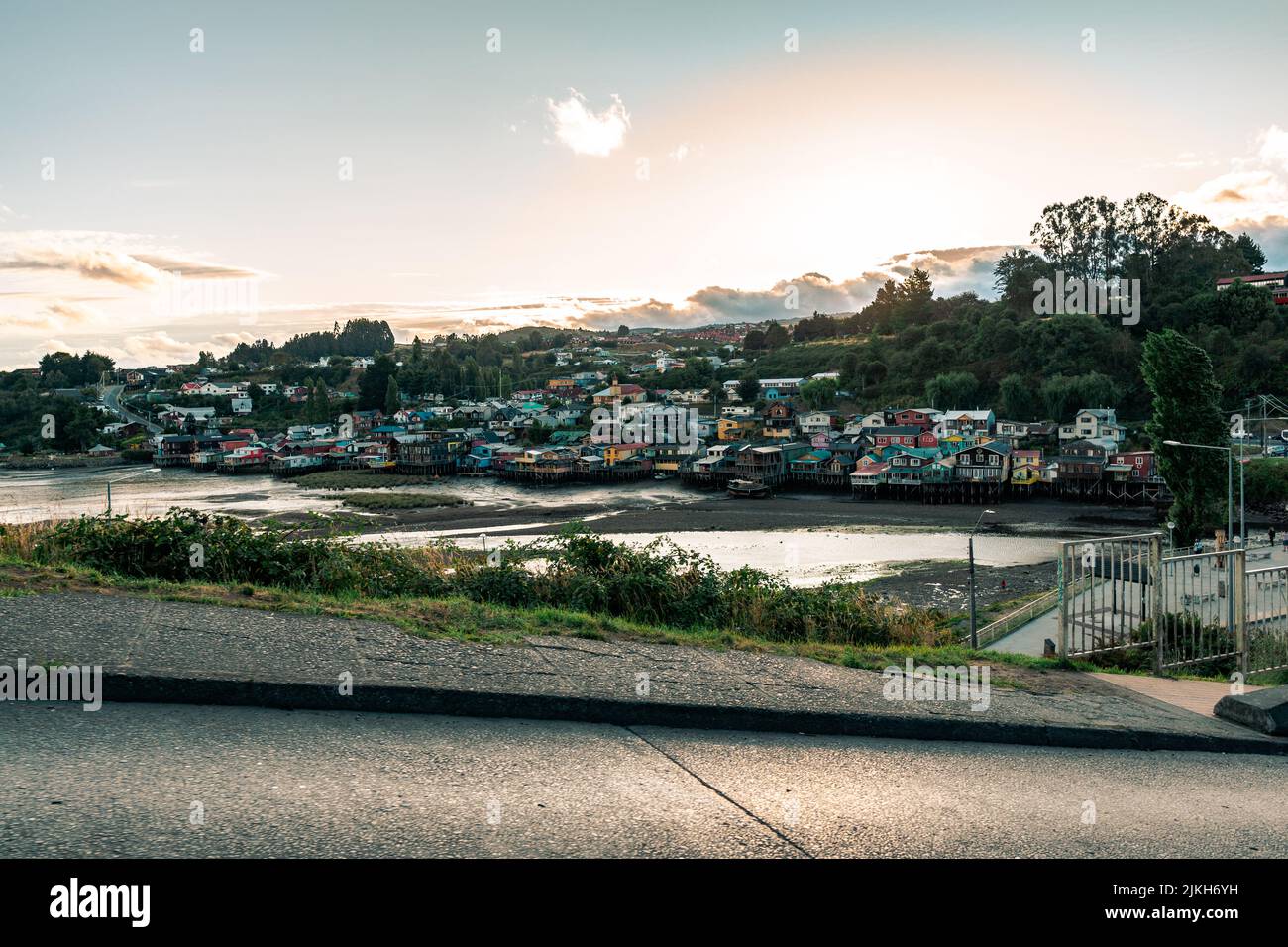 A scenic view of colorful houses and greenery against a lake at sunset ...