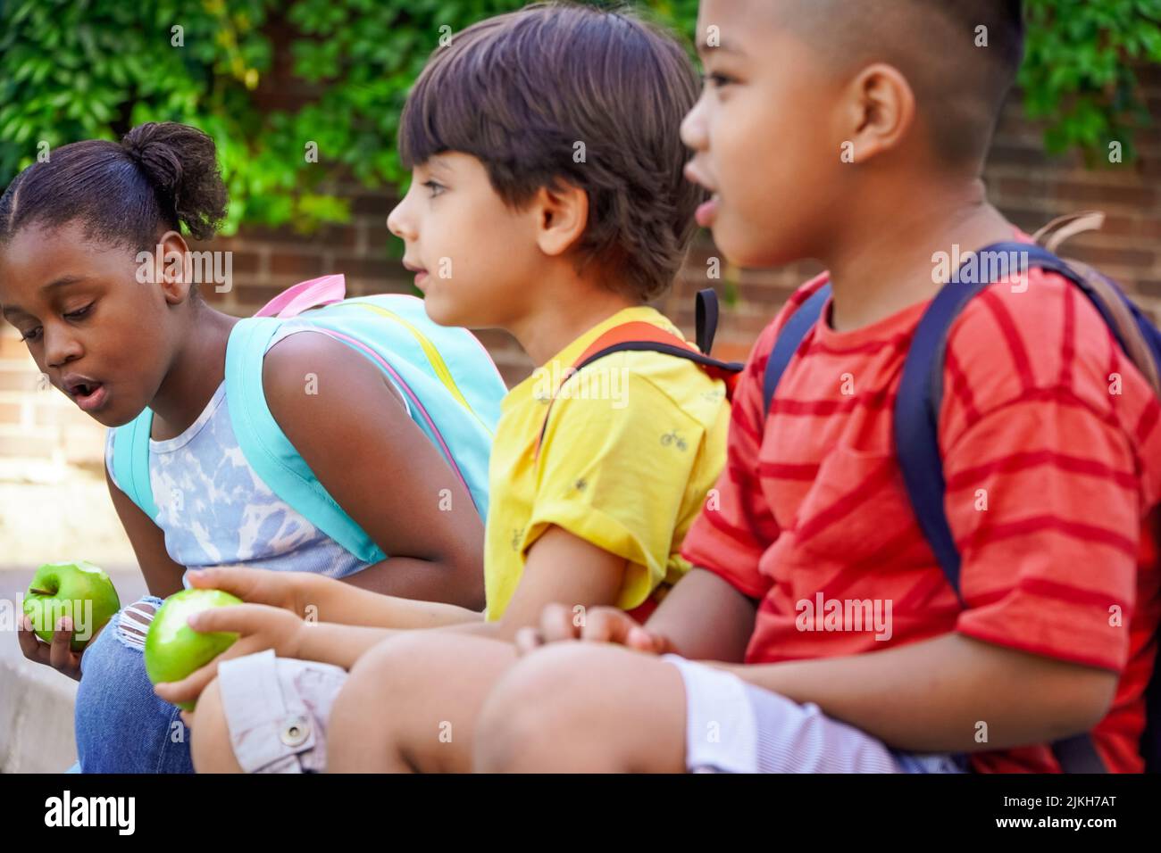 multiethnic kids with backpacks sitting on the street at school ...