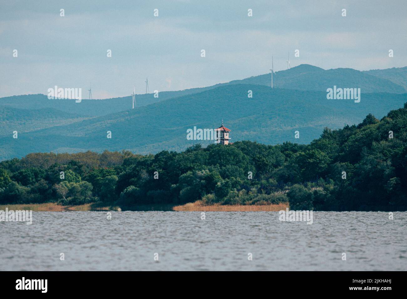 A beautiful view of an old tower in a forest with trees by the lake ...