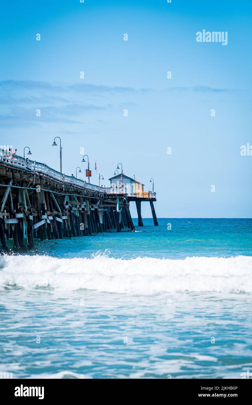 A vertical shot of a wavy and foamy sea and a pier in San Clemente, CA ...