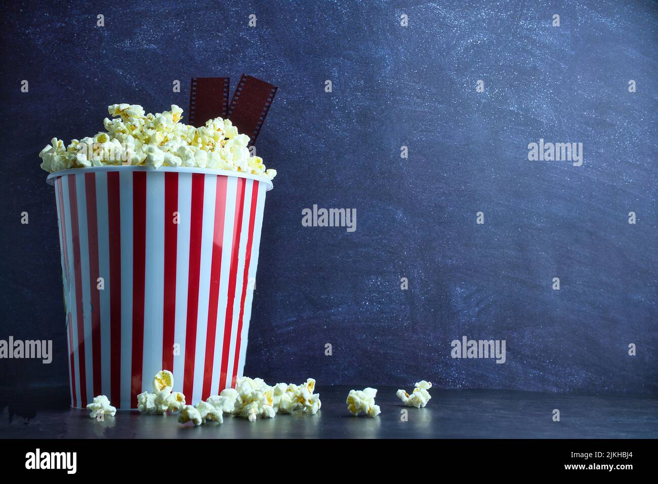 A bucket of popcorn with film strips on a blue background with copy ...