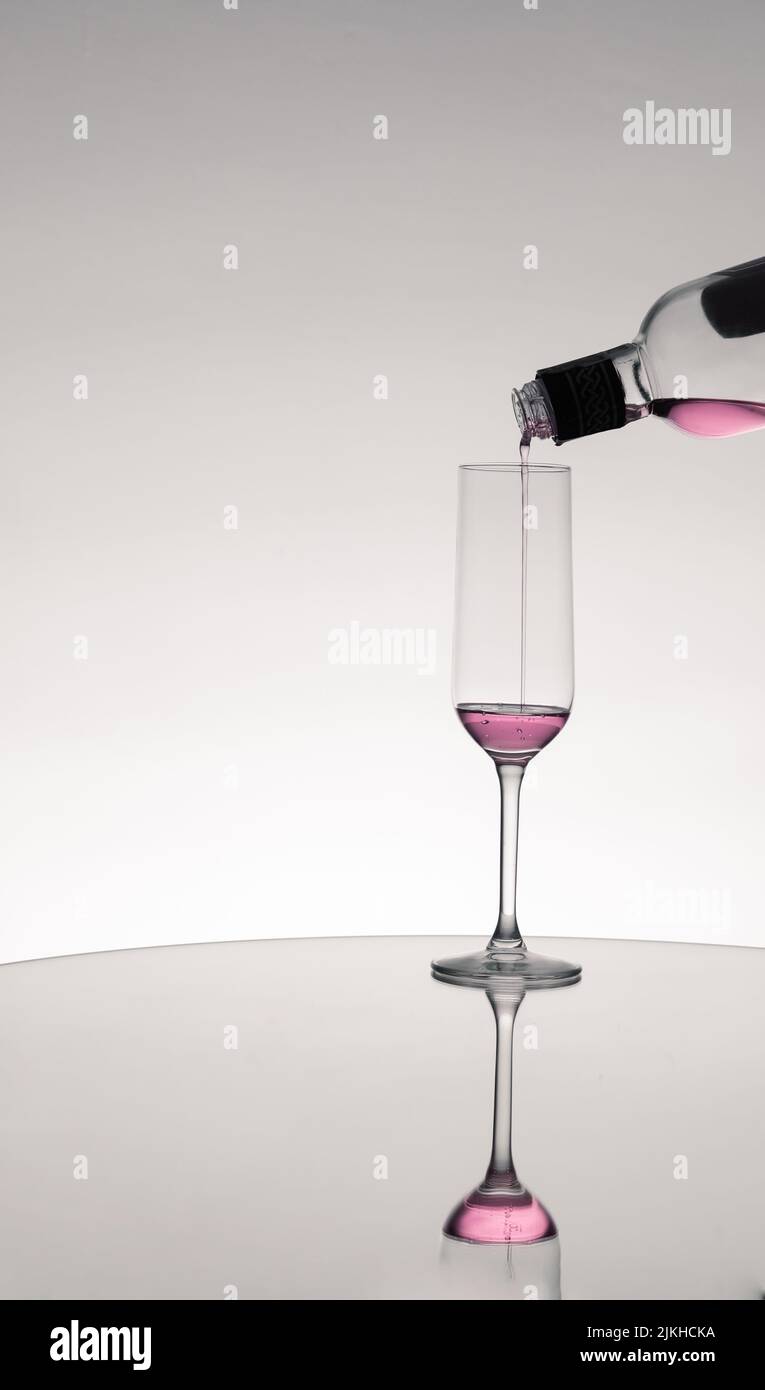 An alcohol drink pouring from a bottle to glass cup with reflection on ...