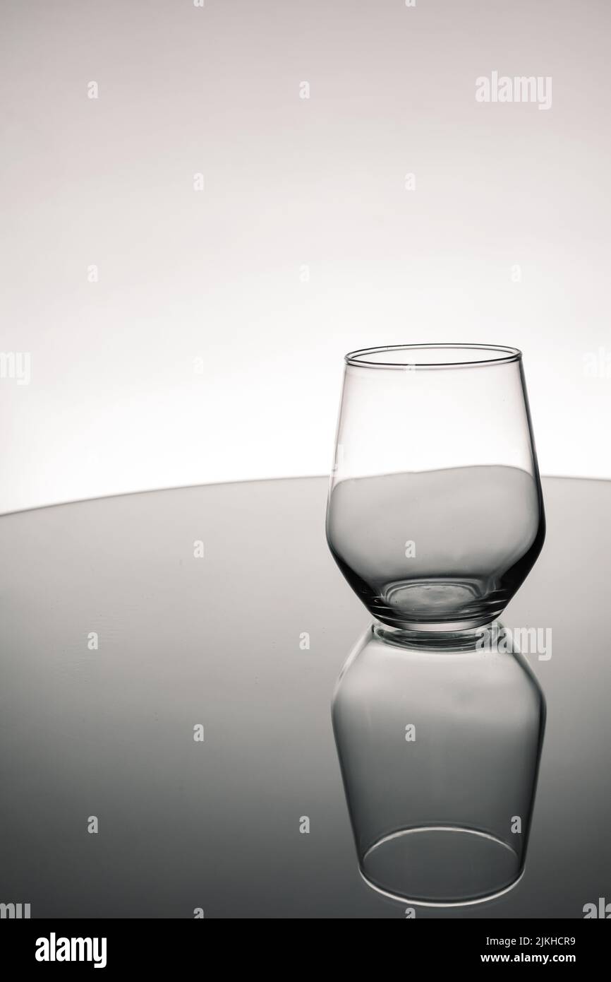 A grayscale shot of an empty glass cup with reflection on a mirror ...
