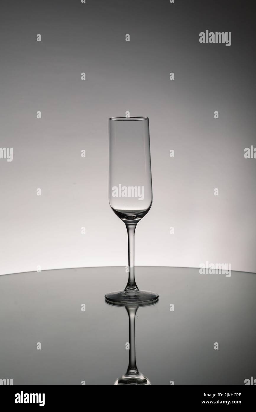 A grayscale shot of an empty glass cup with reflection on a mirror ...