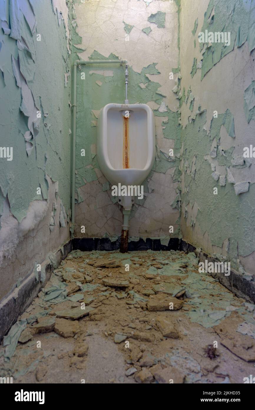 A vertical shot of an old rusty urinal in an abandoned and destroyed ...