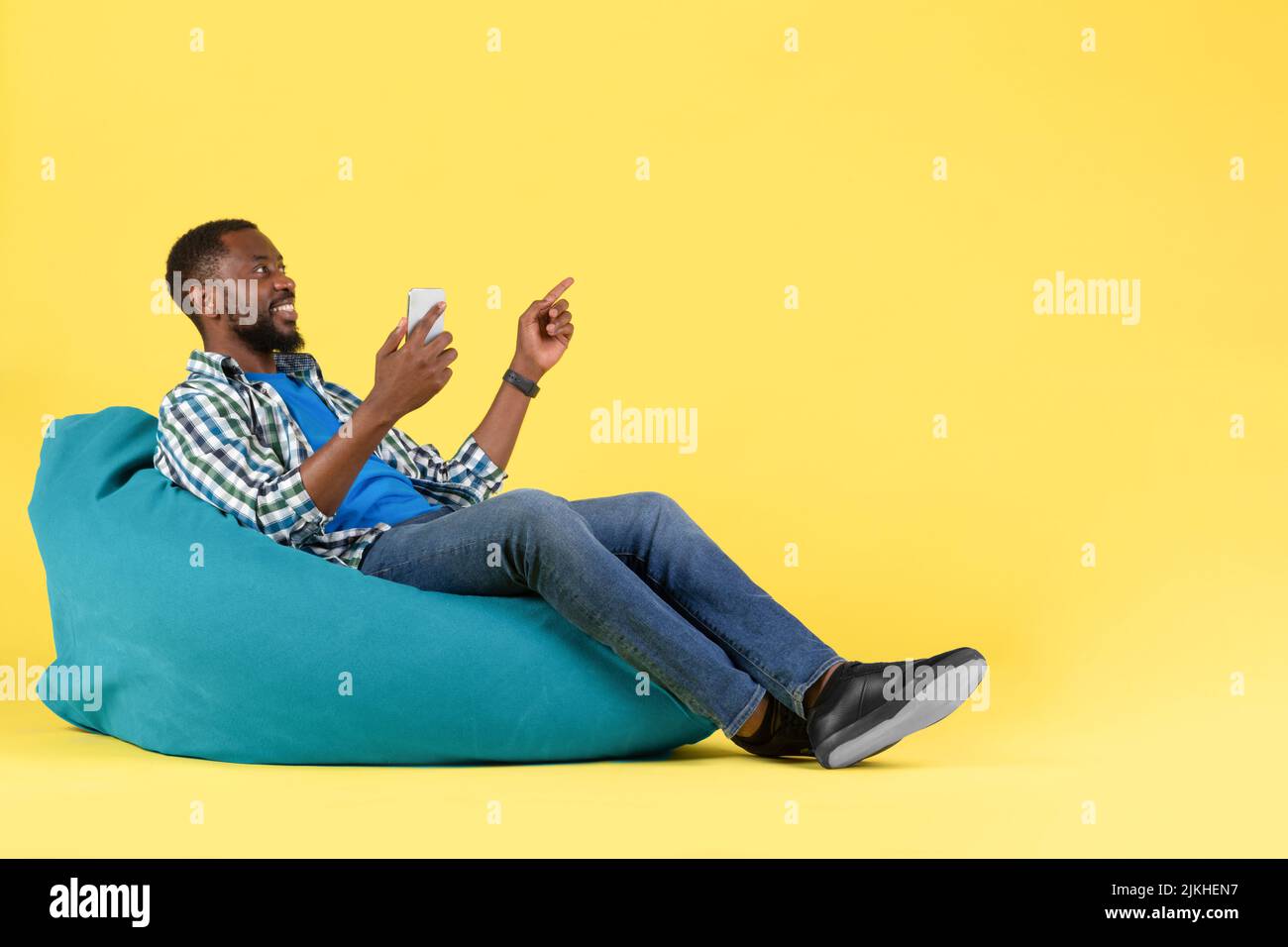 Black Man Using Phone Pointing Finger Sitting Over Yellow Background ...