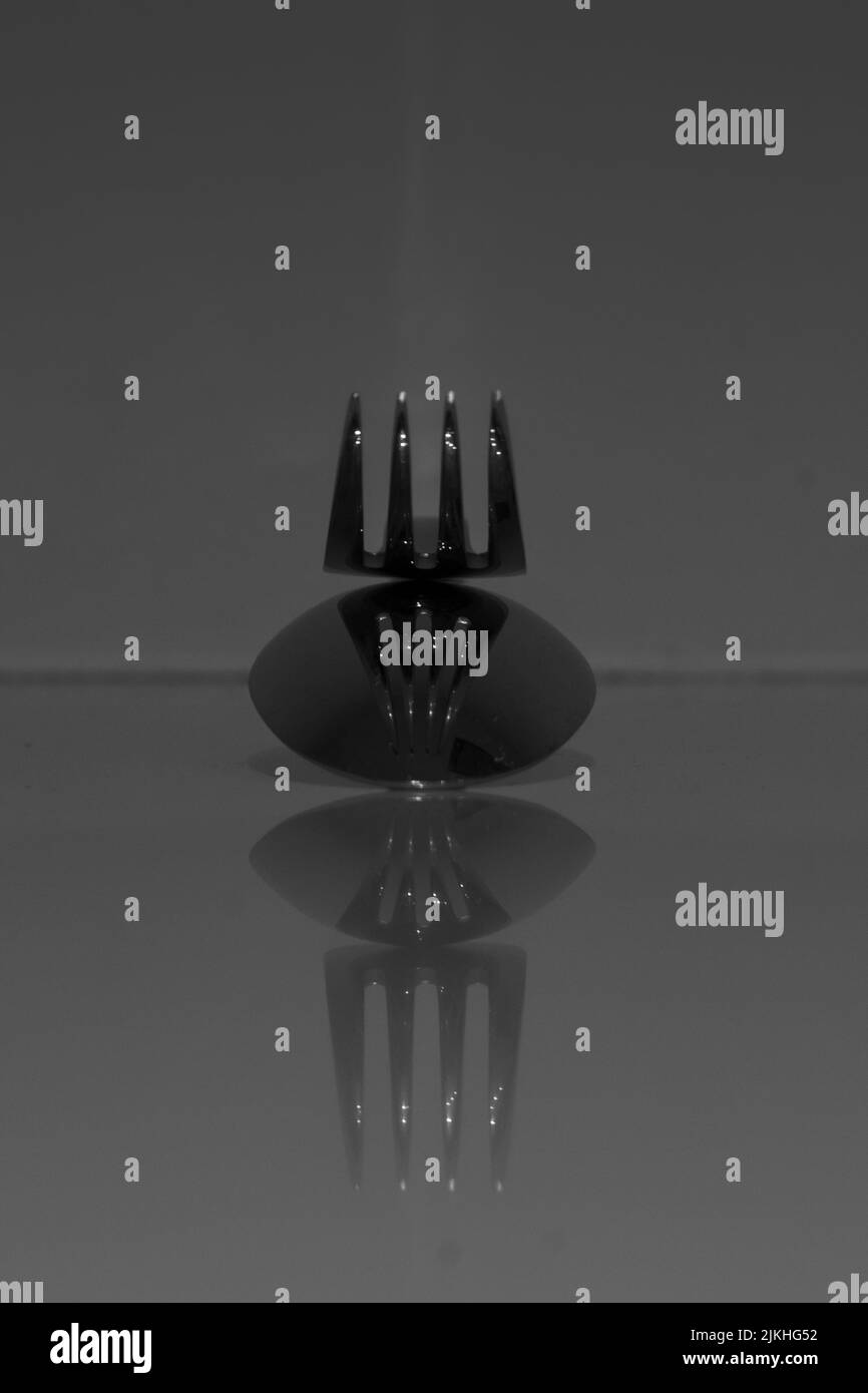 A vertical closeup of a silver fork on a spoon on a reflective ...