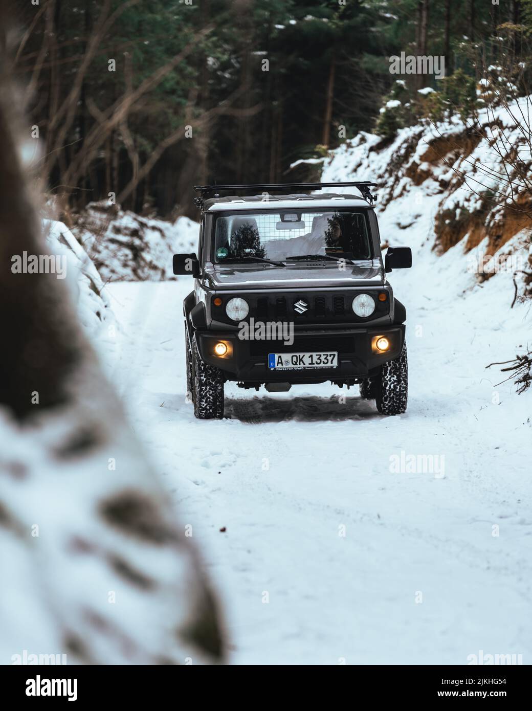A vertical shot of black Suzuki Jimny driving through the woods in ...