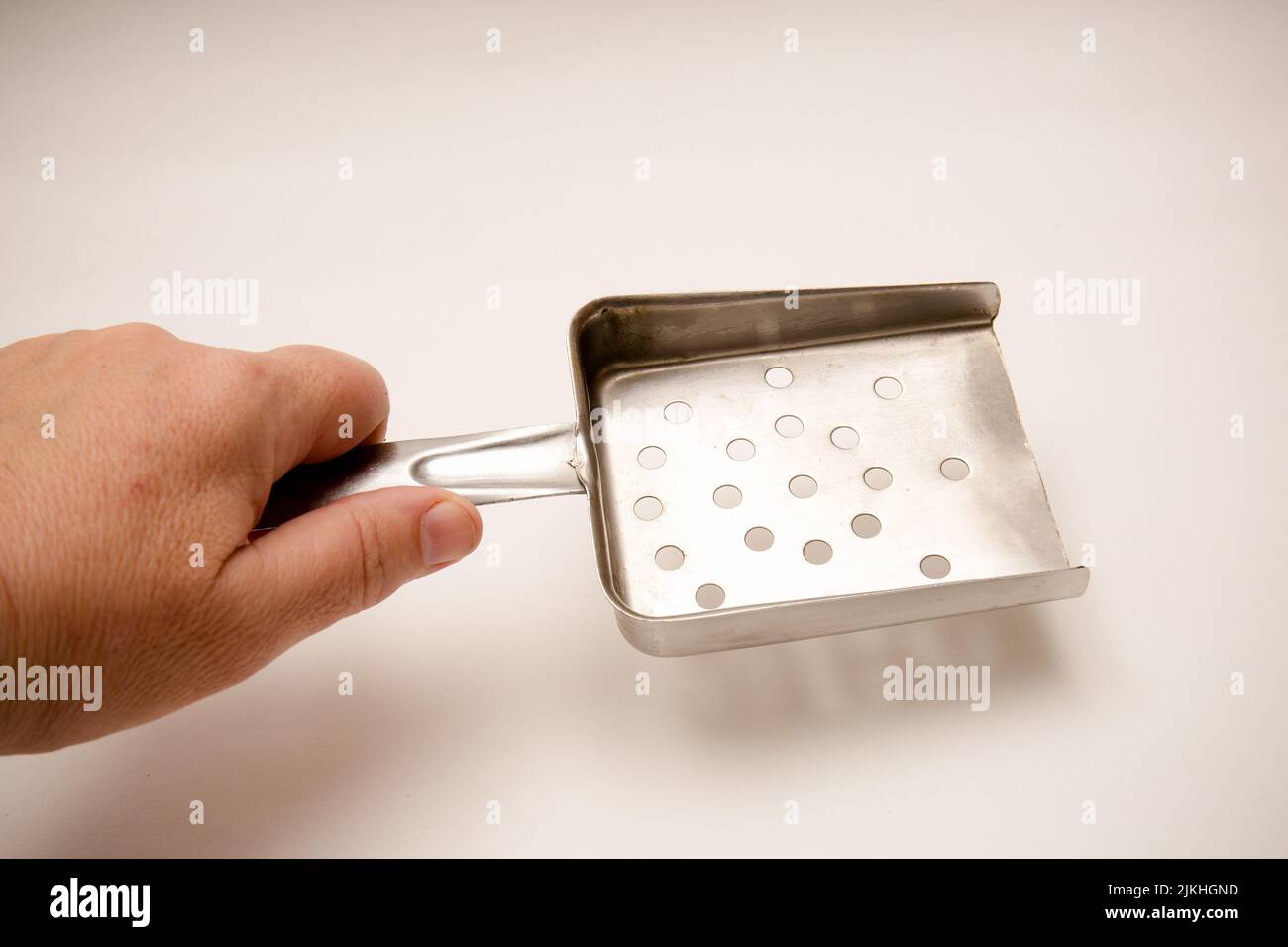 A hand holding a stainless tubular handled chip scoop on isolated white ...