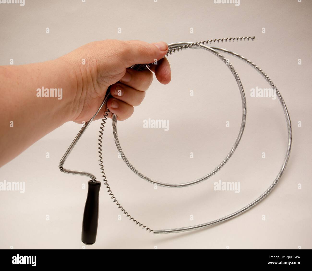 A hand holding a spiral drain unblocker on isolated white background ...
