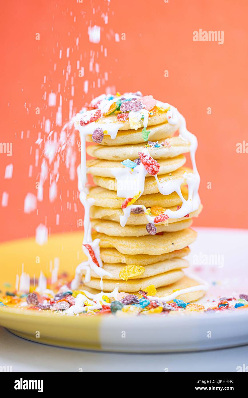 A vertical shot of pancakes with colorful cereal and whipped cream ...