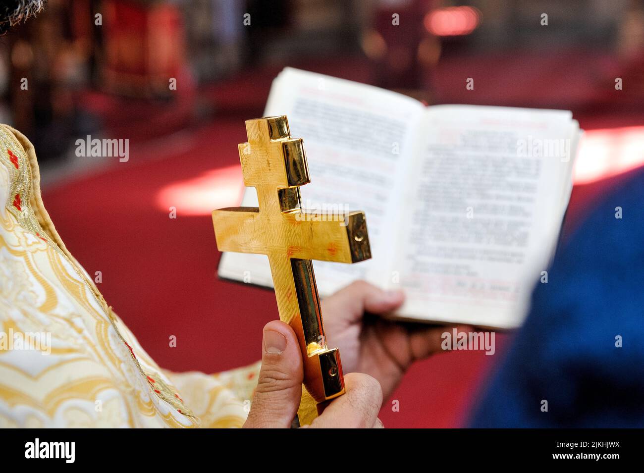 A closeup of a priest's hand holding a golden cross over the bible on a ...