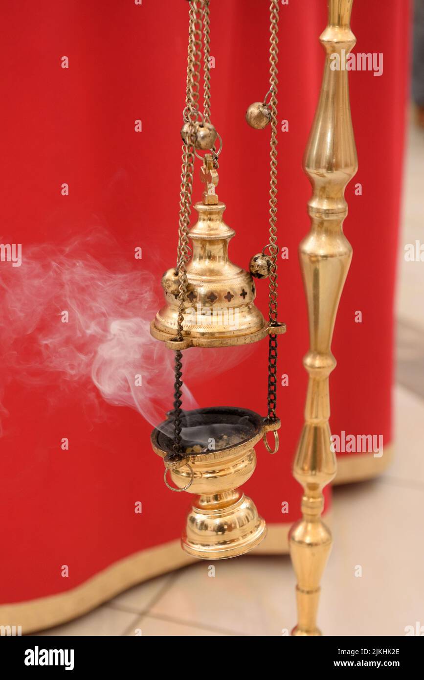 A vertical shot of an open burning censer hanging from a golden stand ...