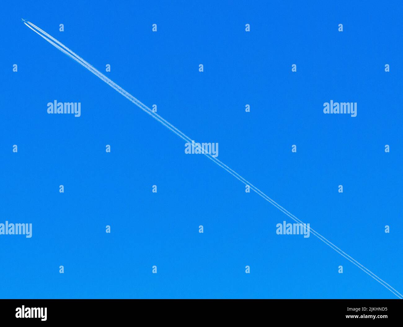 A low angle shot of a long plane trail in the bright blue summer sky ...