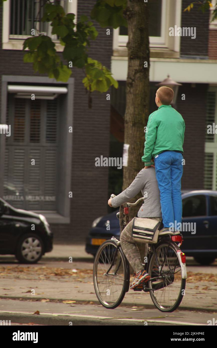 A vertical shot of Caucasian kids seen from behind, riding a bicycle on ...