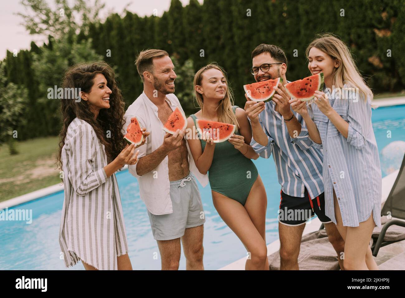 Group of young people standing by the swimming pool and eating ...