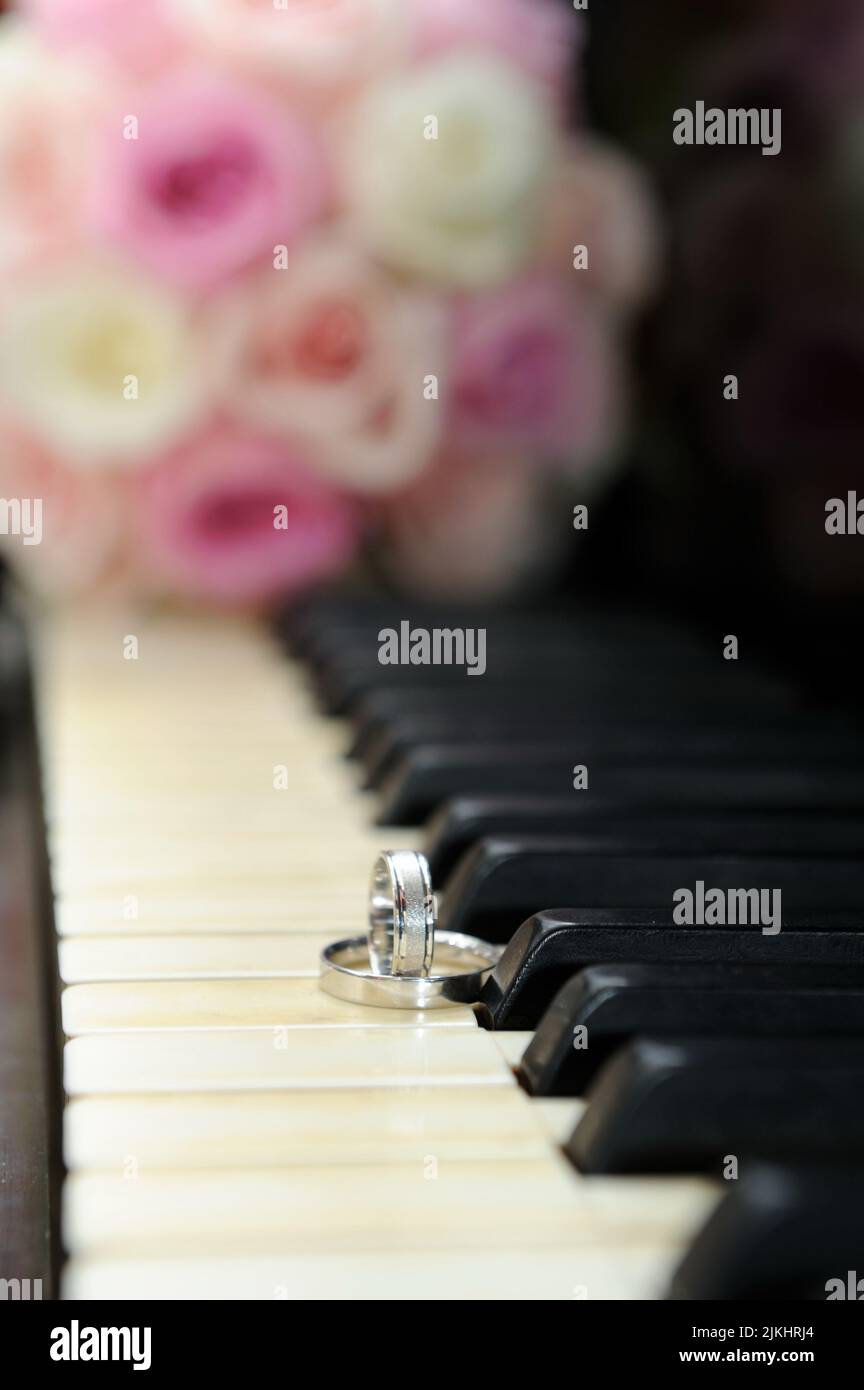 A vertical shot of the wedding rings on the piano keys with the bouquet ...