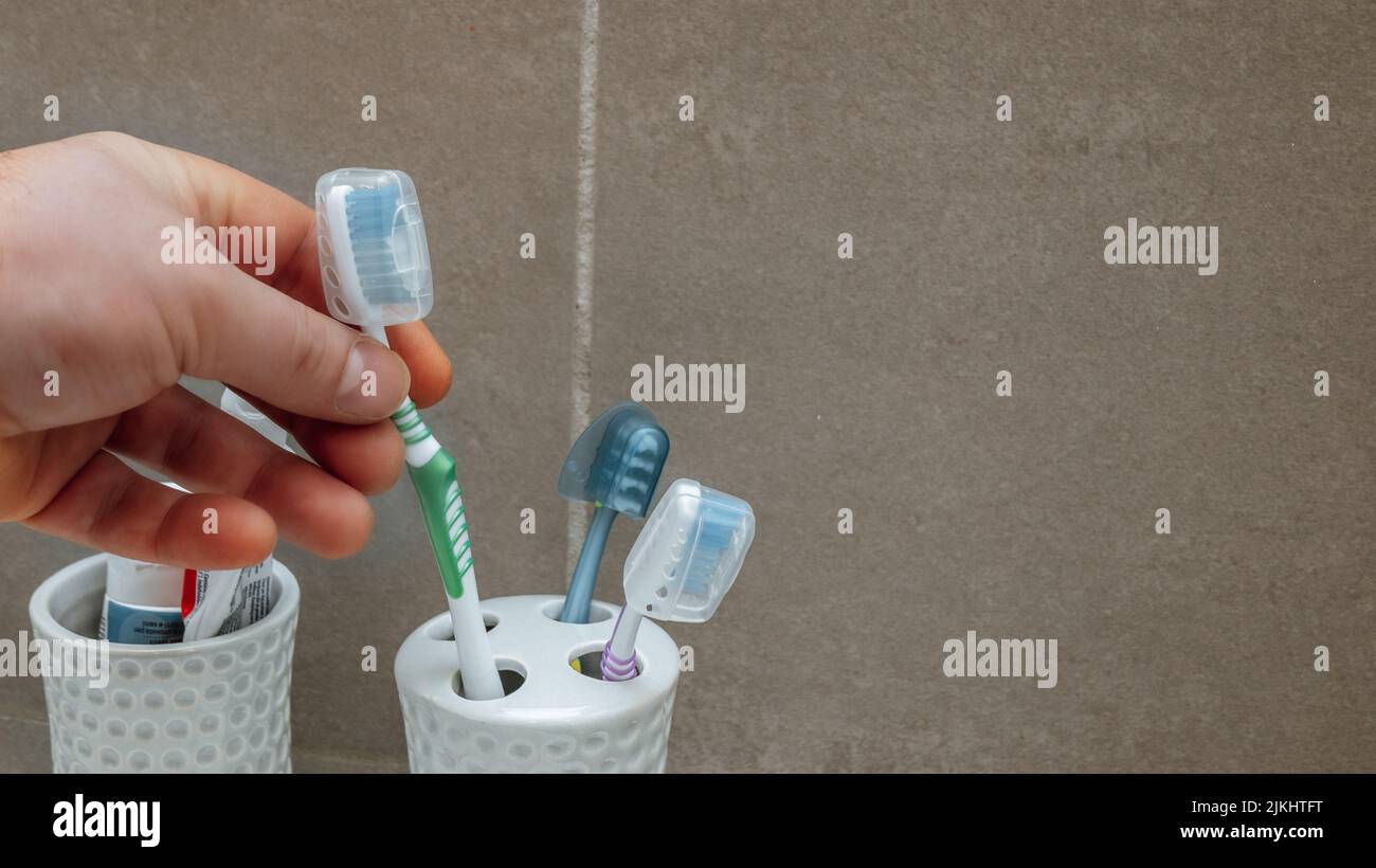 The man pulls a toothbrush from the holder. Hand on the left side of ...