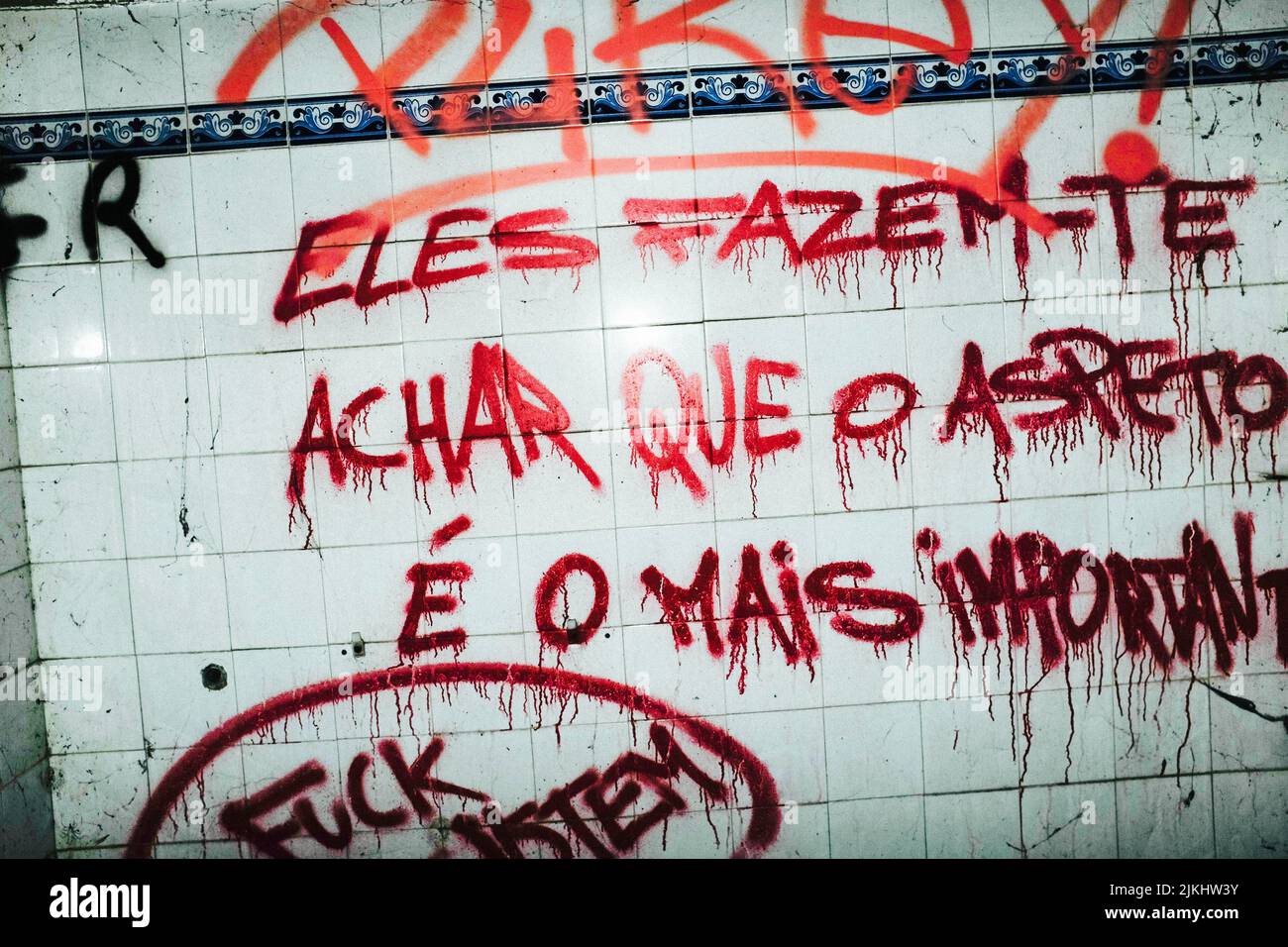 Red graffiti words in Portuguese painted on an old dirty white tiled ...