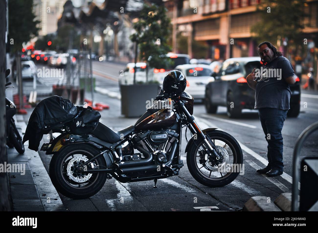 A biker posing next to a motorcycle parked on the side of the road in ...