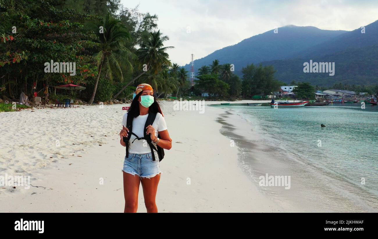 A Caucasian female in a face mask and with a backpack walking on the ...