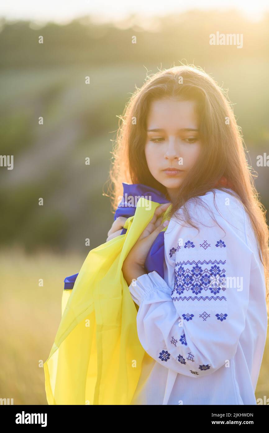 A sad teenage girl holds a Ukrainian flag to her chest. The girl is ...