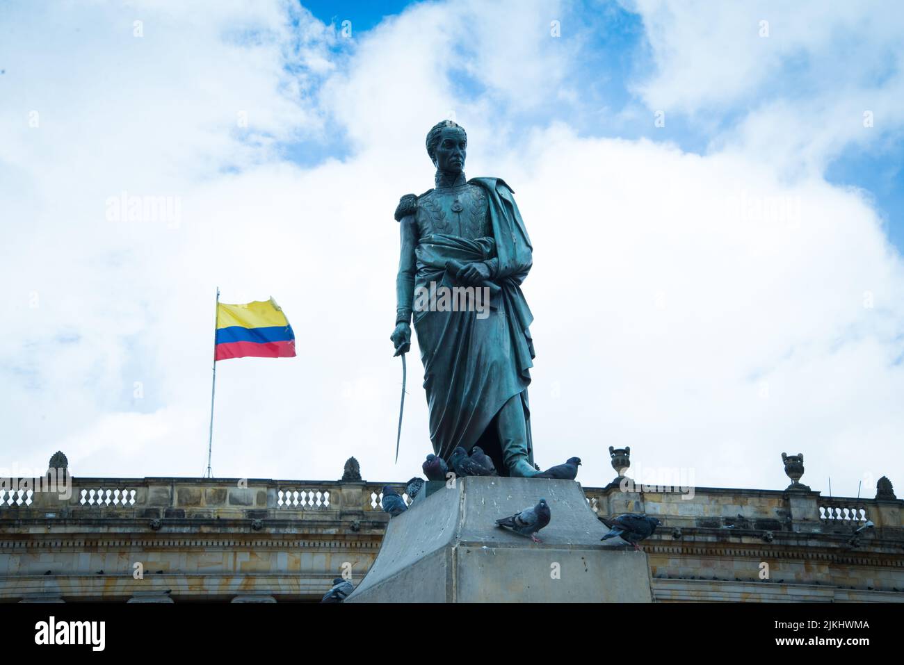 A beautiful view of a statue and Colombian flag under the blue cloudy ...