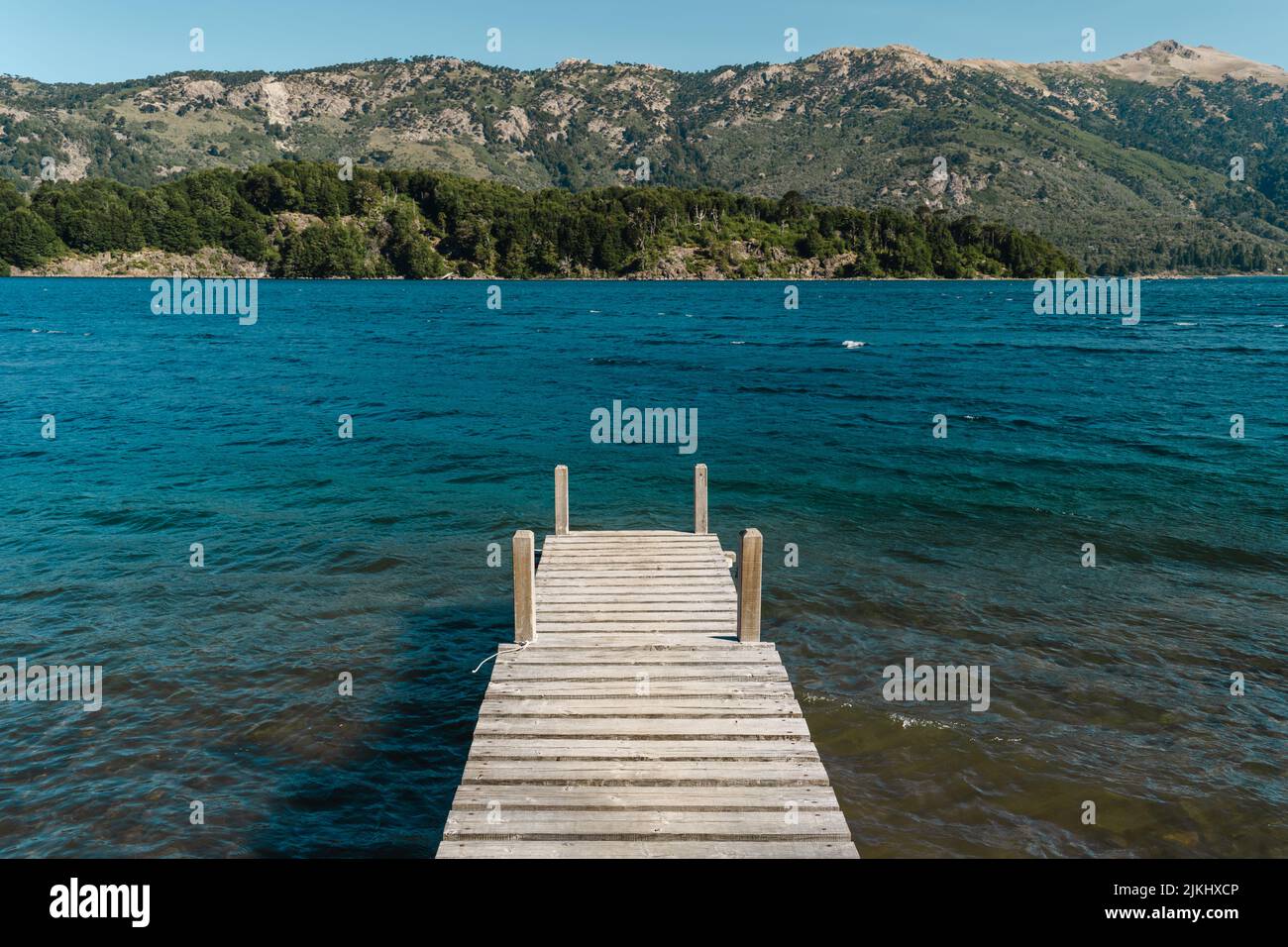 A view of a wooden jetty above the calm sea with mountains in the ...