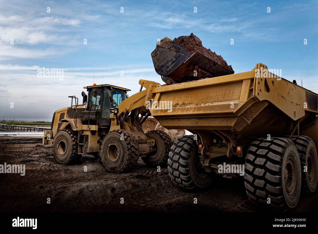 A number of dump trucks loaded with dirt in the cloudy sky background ...