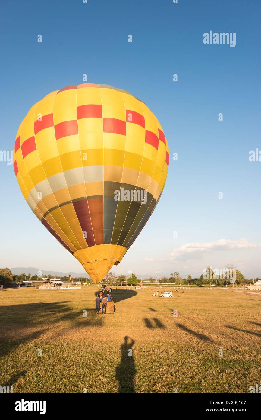 A vertical shot of a yellow hot air balloon in a field against a blue ...