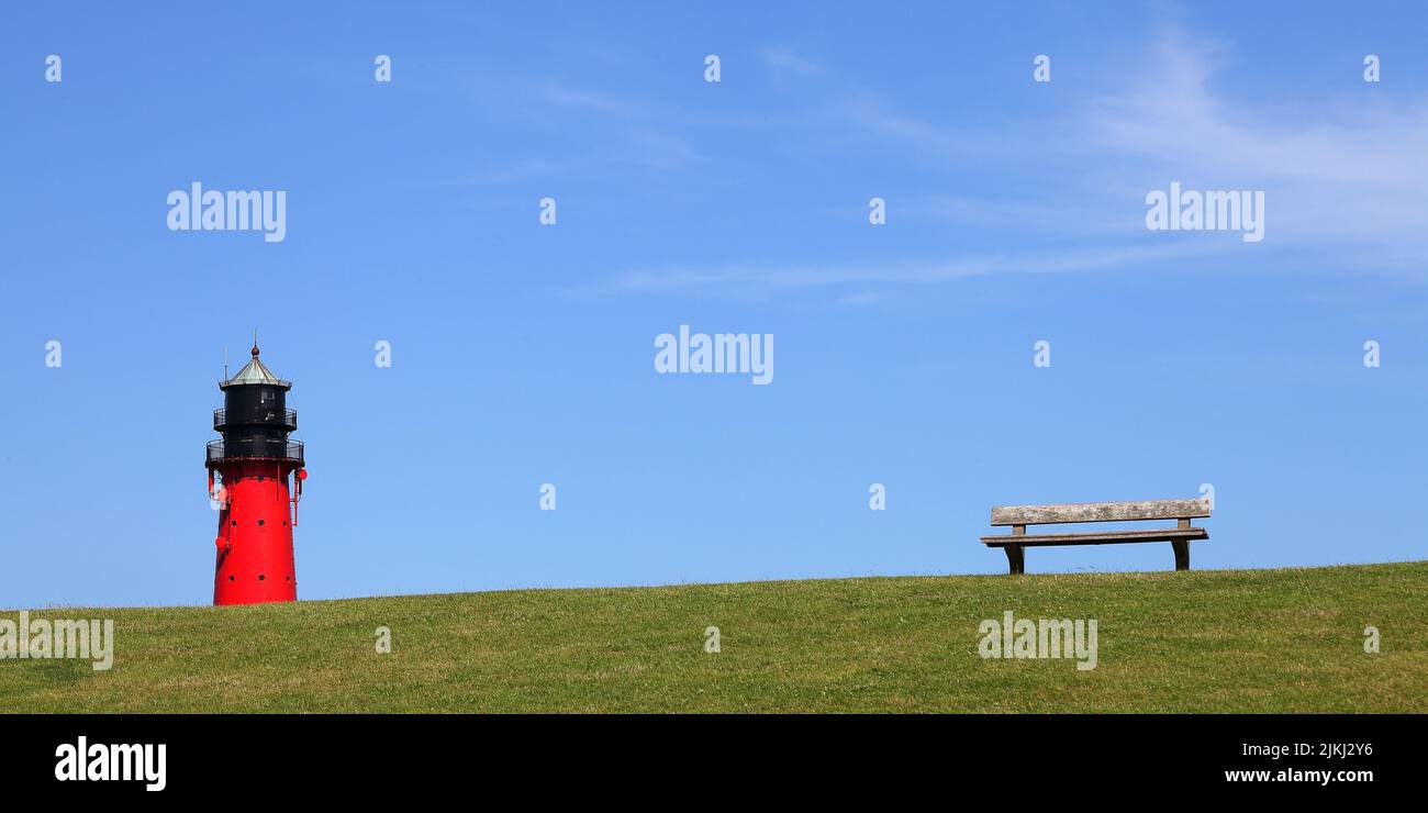 A closeup of a red lighthouse in a green field with a bench Stock Photo ...