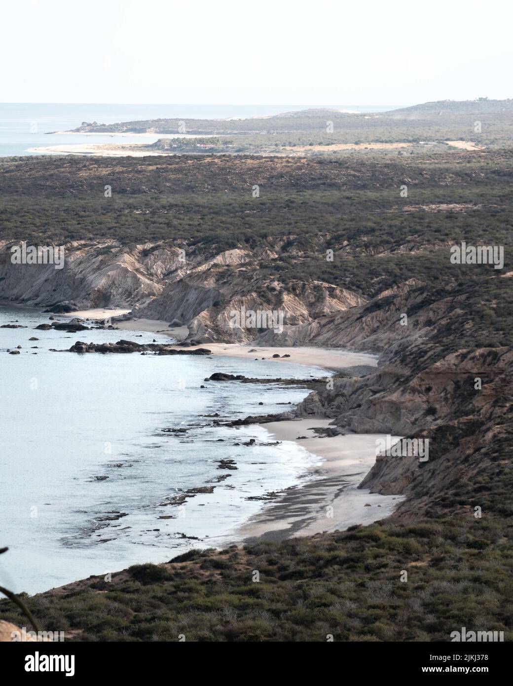 A small sandy beach on the ocean at the foot of small rocks with grass ...