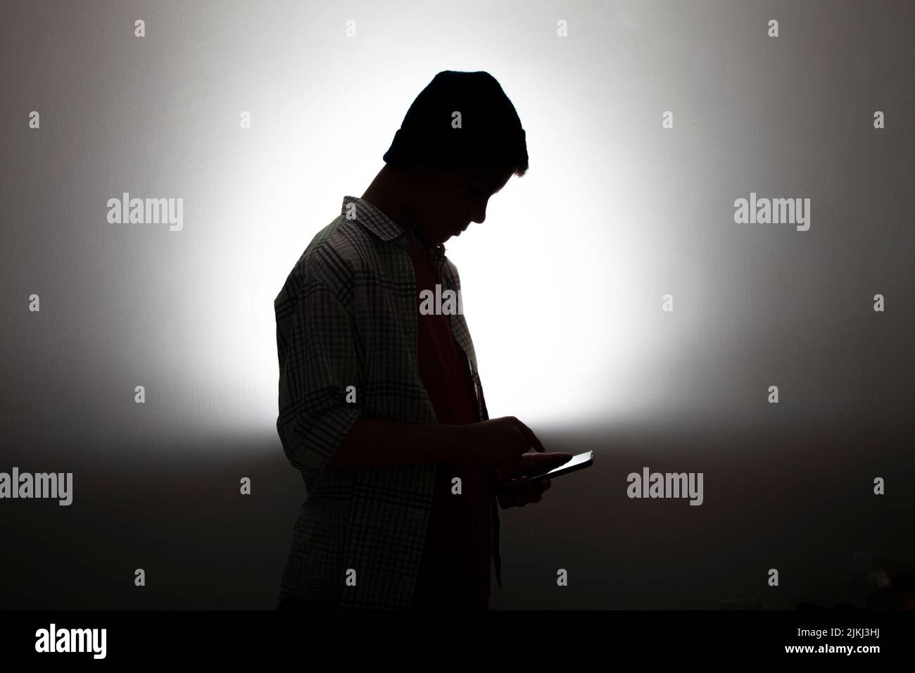 A silhouette view of a young man using his smartphone on a lighting ...