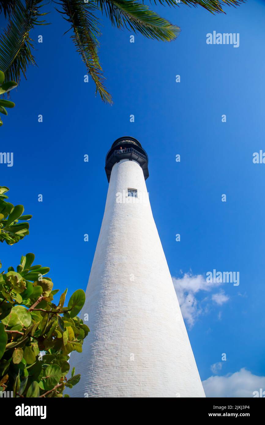 A low angle of the tall white painted lighthouse under the cloudy blue ...