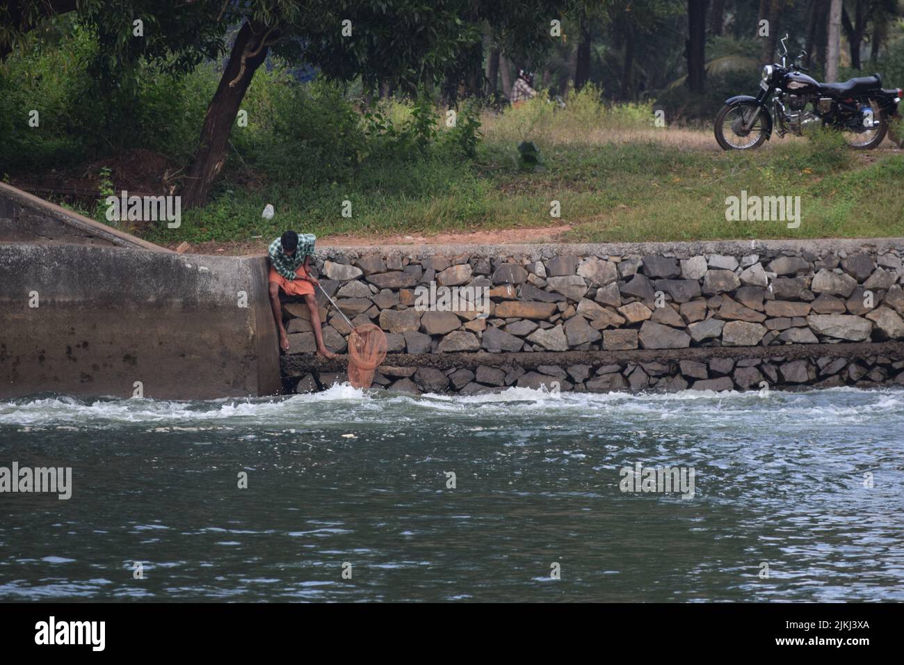 A male fishing in the river and a motorbike parked on the grass in ...