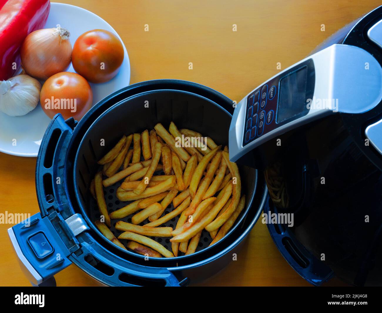 Top view of an air fryer on a table with french fries and vegetables ...