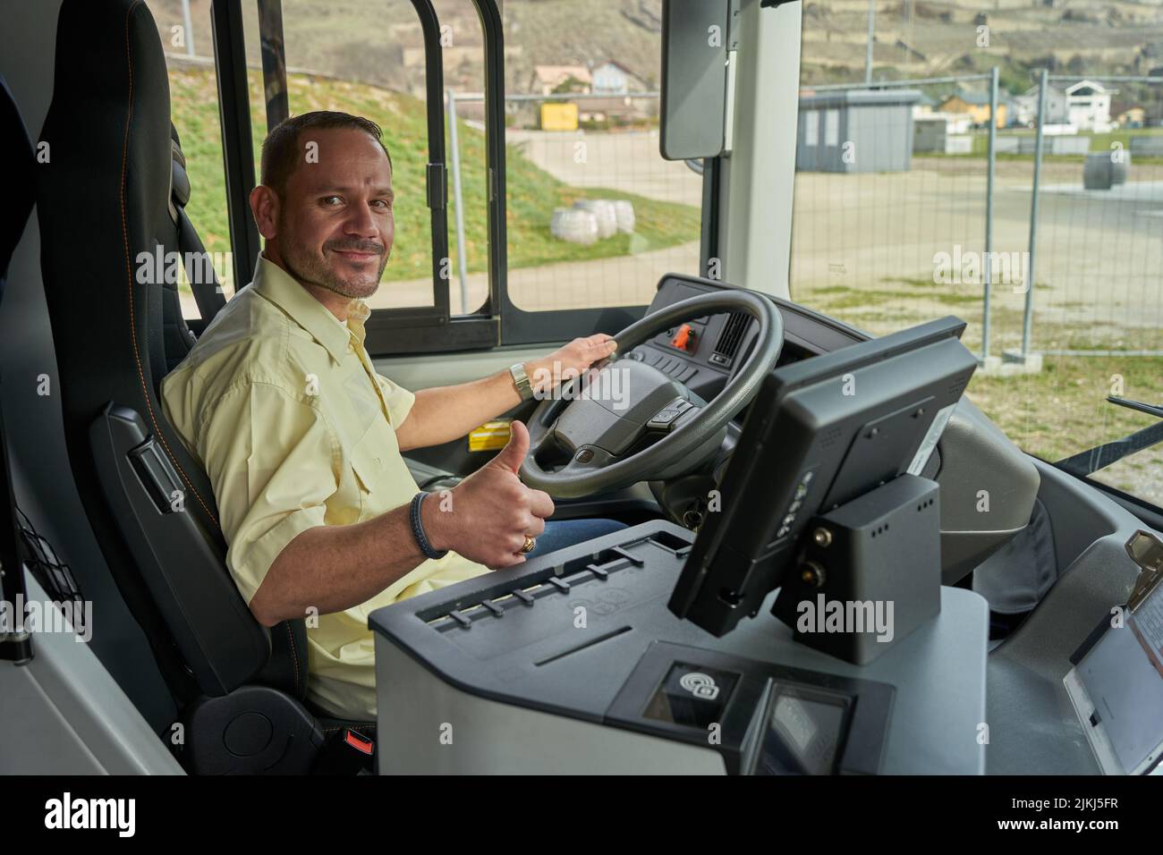 A Hispanic male driving a modern bus in the daylight with a garden ...