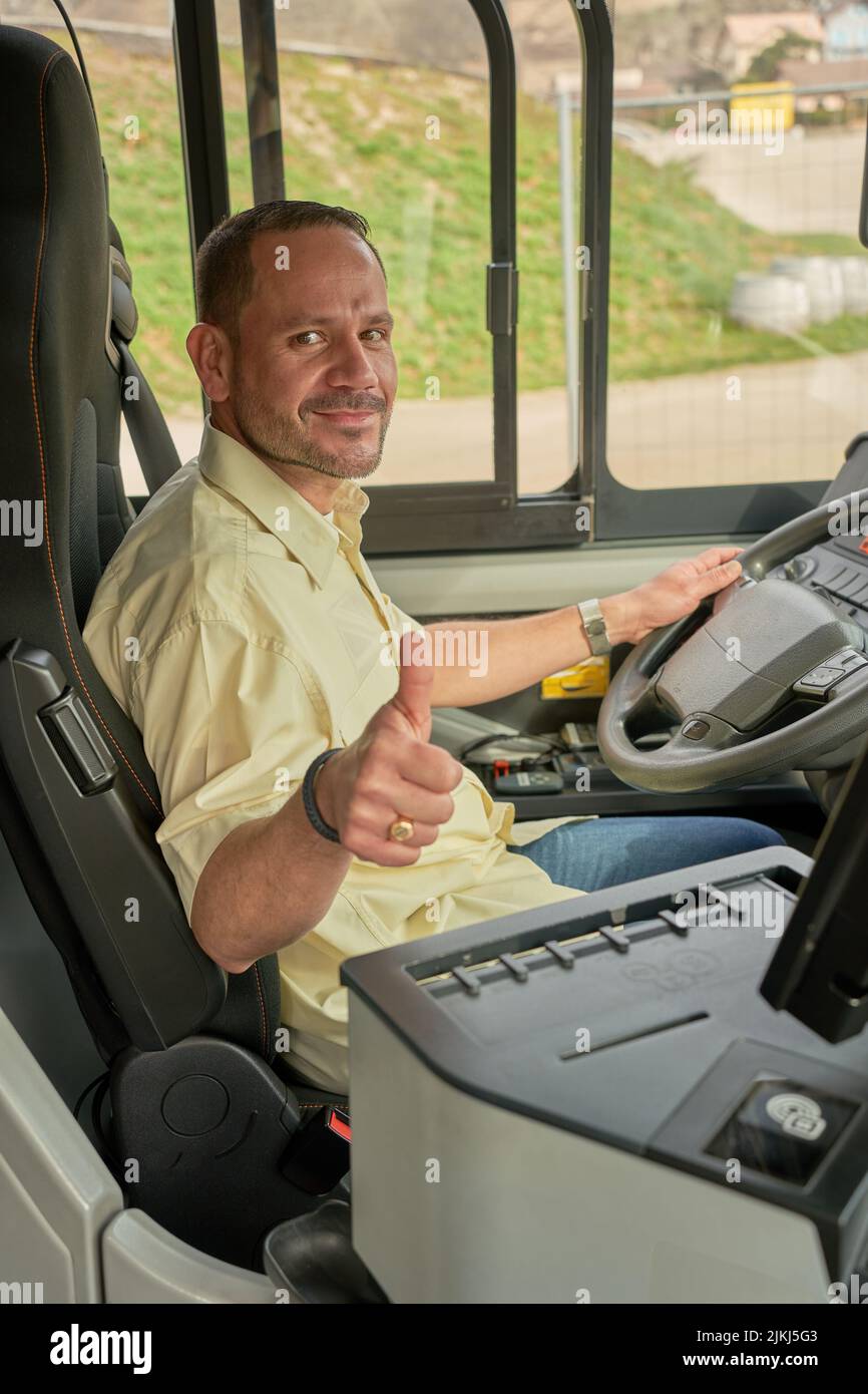 A Hispanic male driving a modern bus in the daylight with a garden ...
