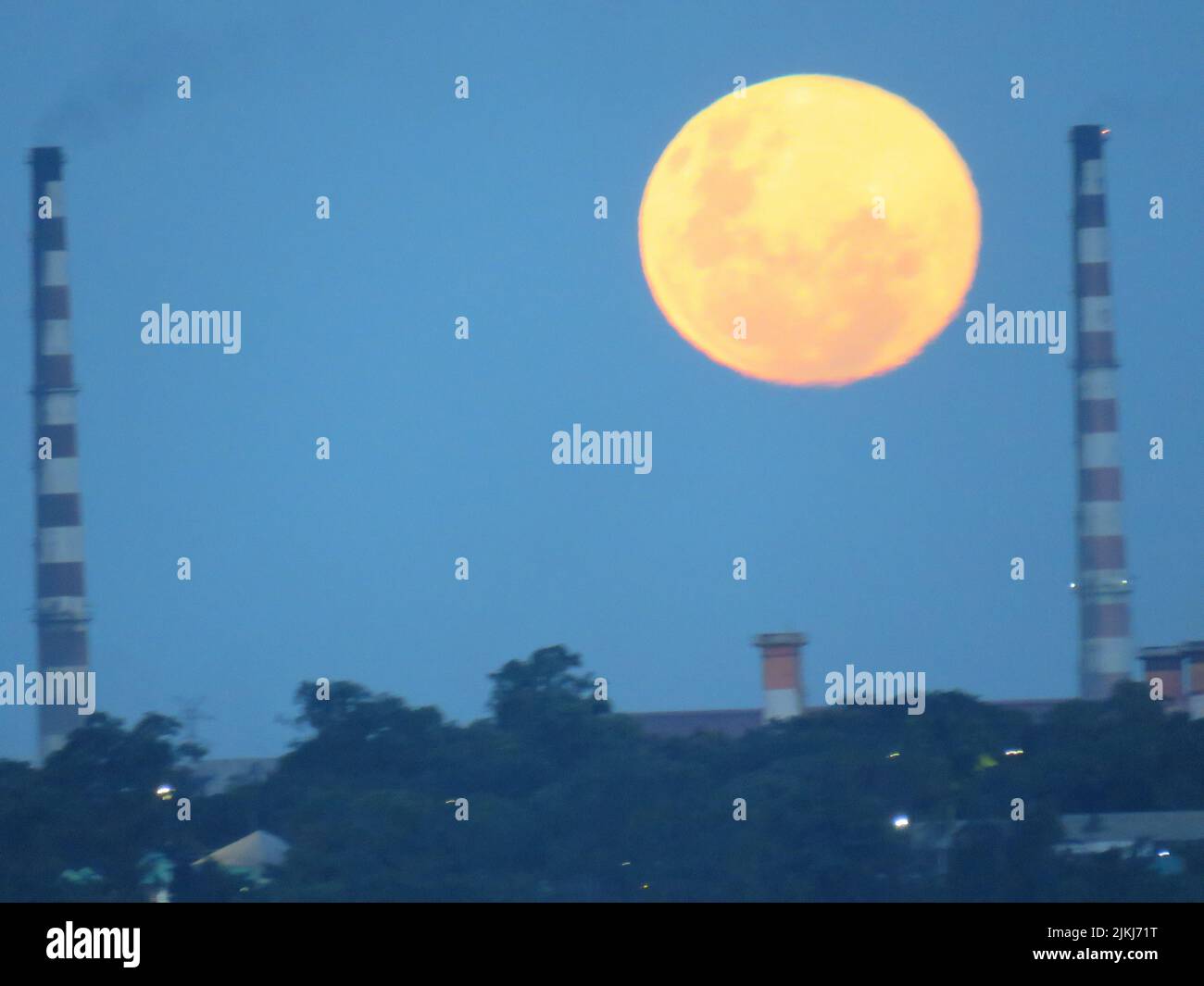 A shot of a yellow full moon behind tall industrial chimneys with a ...