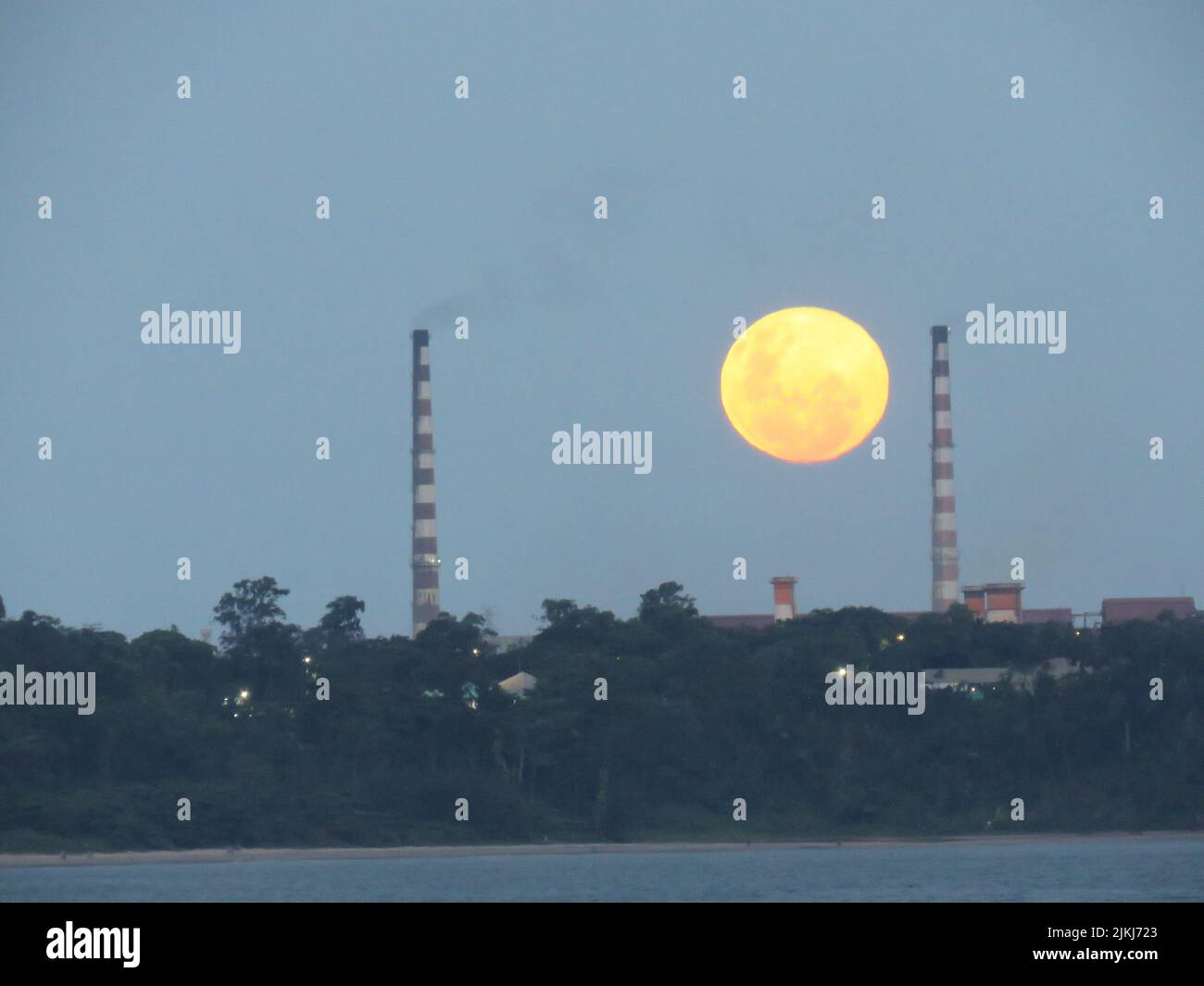 A shot of a yellow full moon behind tall industrial chimneys with a ...
