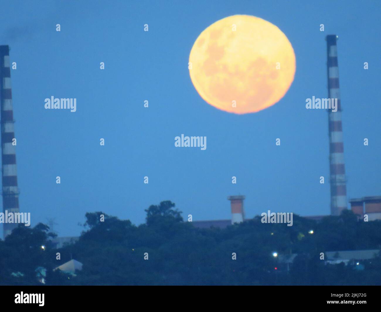 A shot of a yellow full moon behind tall industrial chimneys with a ...