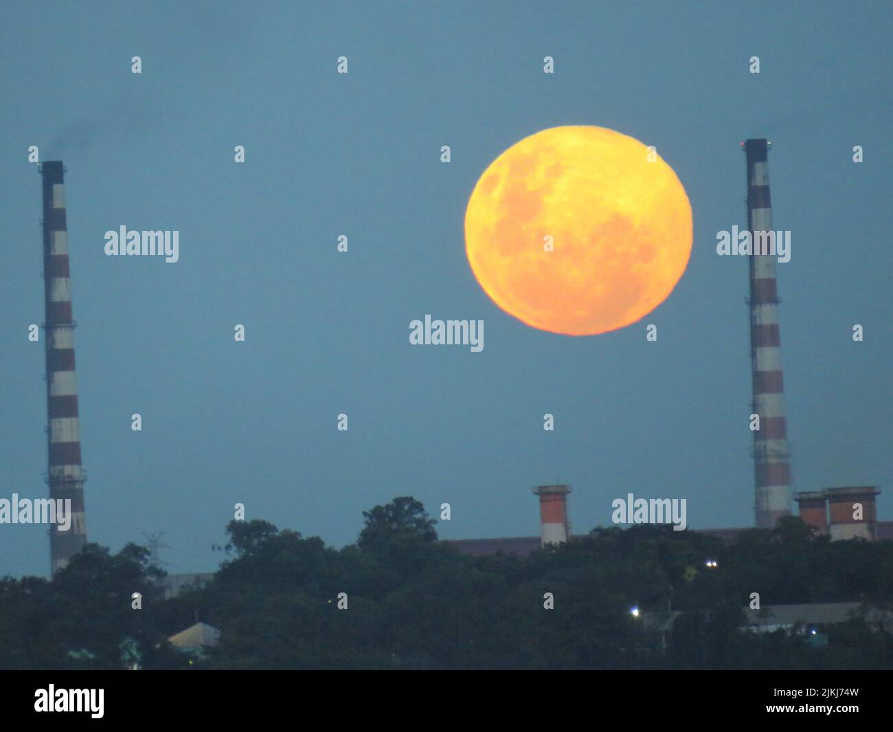A shot of a yellow full moon behind tall industrial chimneys with a ...