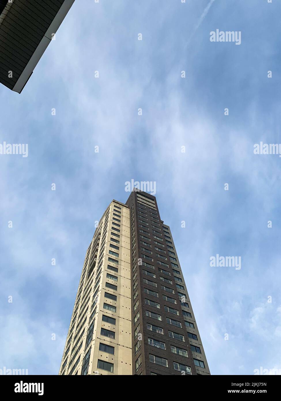 A vertical shot of a modern high rise building against a blue cloudy ...