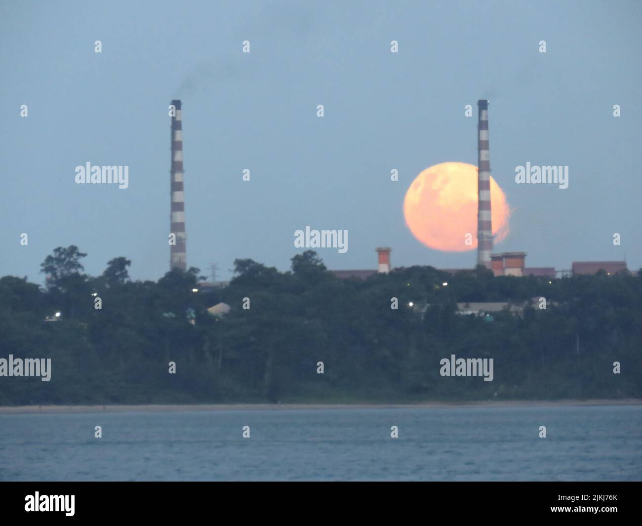 A shot of a yellow full moon behind tall industrial chimneys with a ...