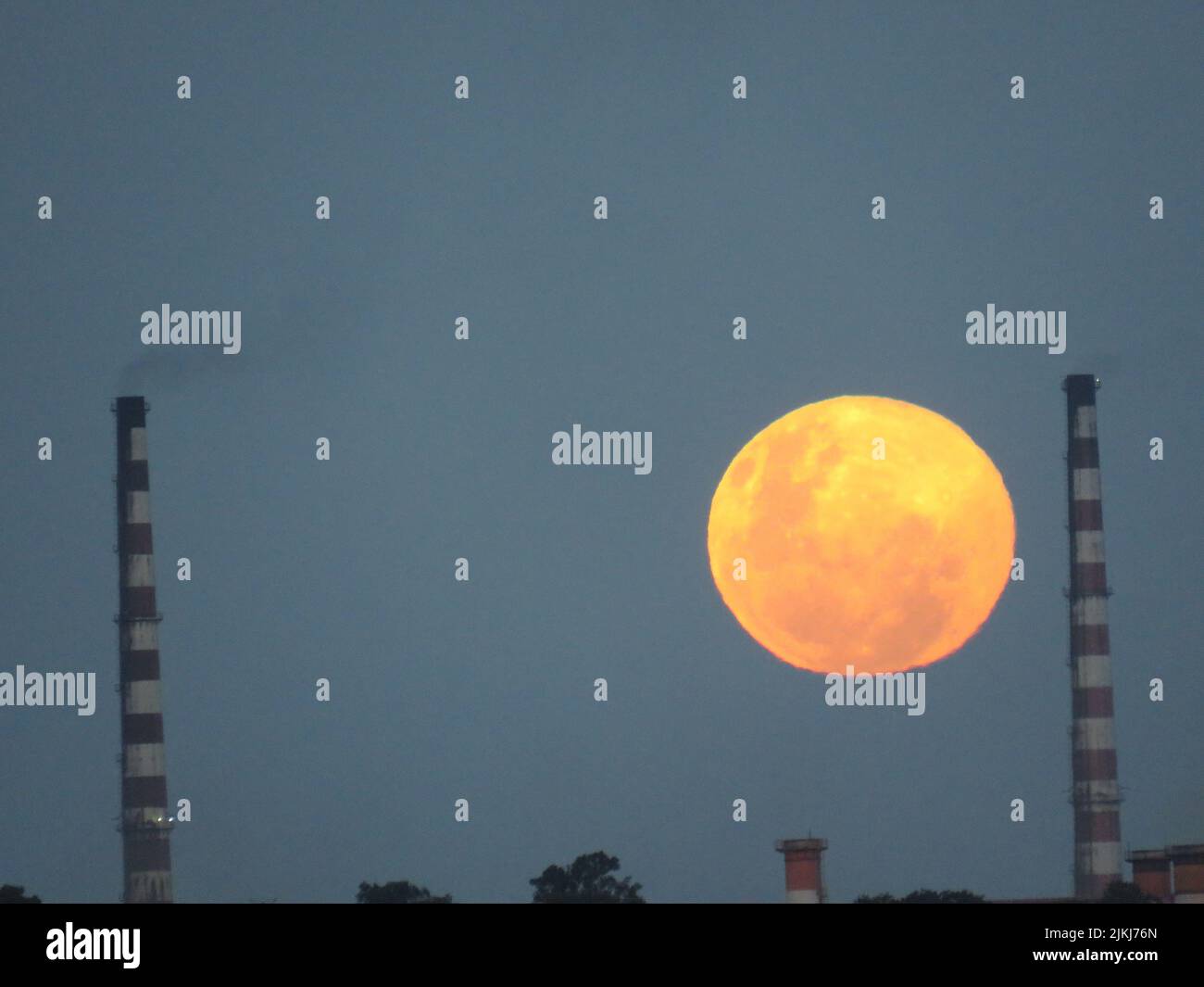 A shot of a yellow full moon behind tall industrial chimneys Stock ...