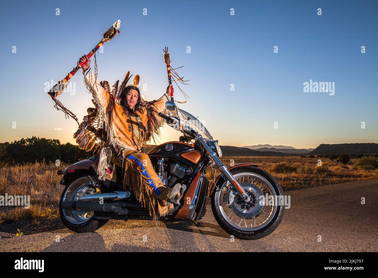 Traditionally dressed Native American man holds up two coup sticks ...