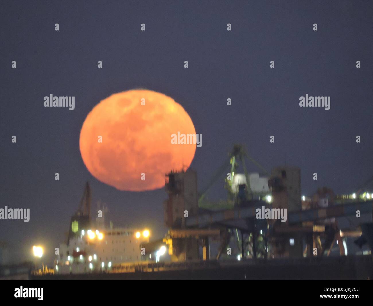 A shot of a bright yellow supermoon with a foreground of a cargo ship ...
