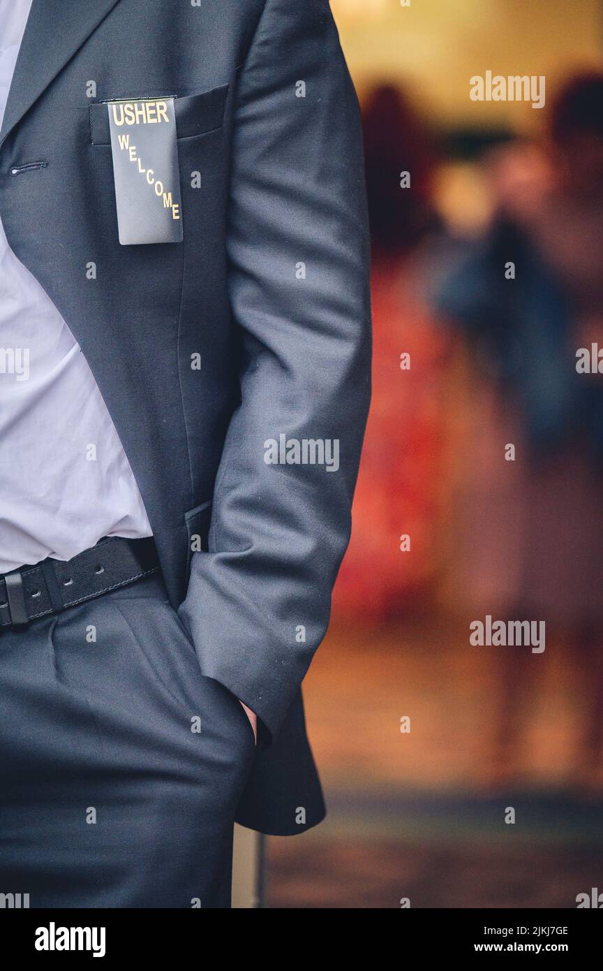 A vertical shot of a male event usher in a gray suit against a blurred ...